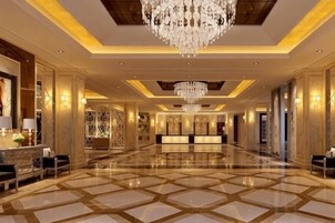 Um hall espaçoso com piso de mármore polido, um lustre imponente e um balcão de recepção.