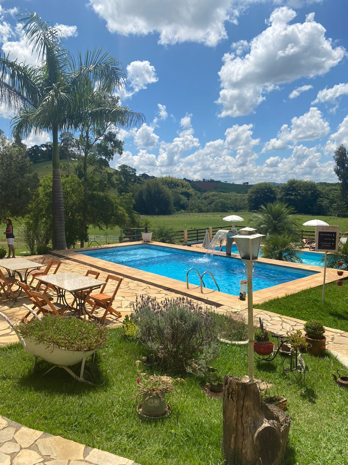 Uma piscina com espreguiçadeiras e guarda-sóis, cercada por vegetação e um céu claro.