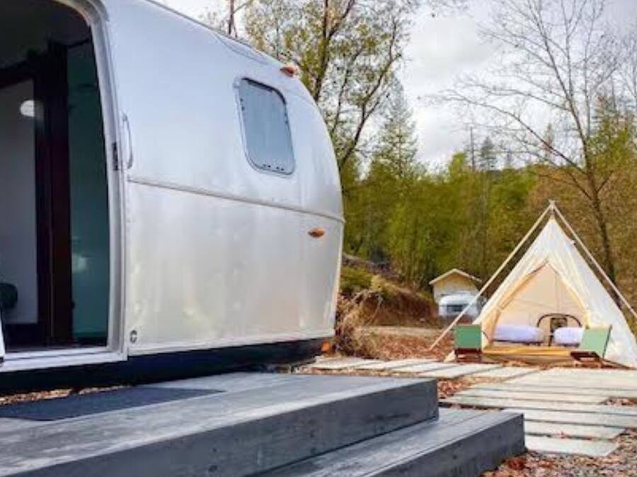Uma RV branca estacionada ao lado de uma pequena tenda.