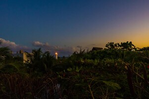 Vista noturna de um edifício com uma torre iluminada, rodeado por vegetação densa e um céu limpo.
