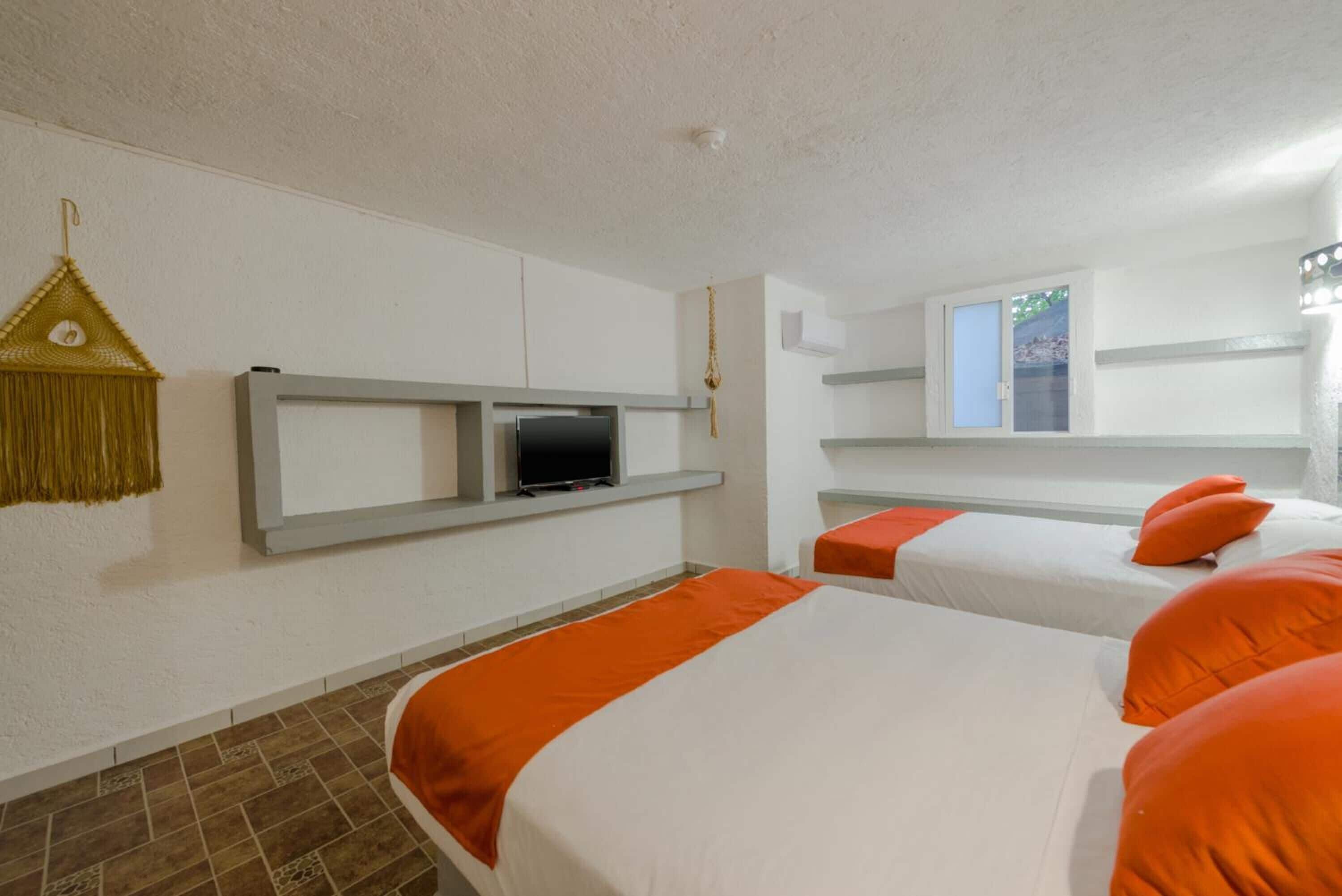 Quarto de hotel com duas camas, uma TV fixada na parede e uma janela com vista para o verde.