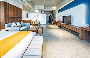 Quarto de hotel moderno com sofá, cama, escrivaninha, televisão e escada.