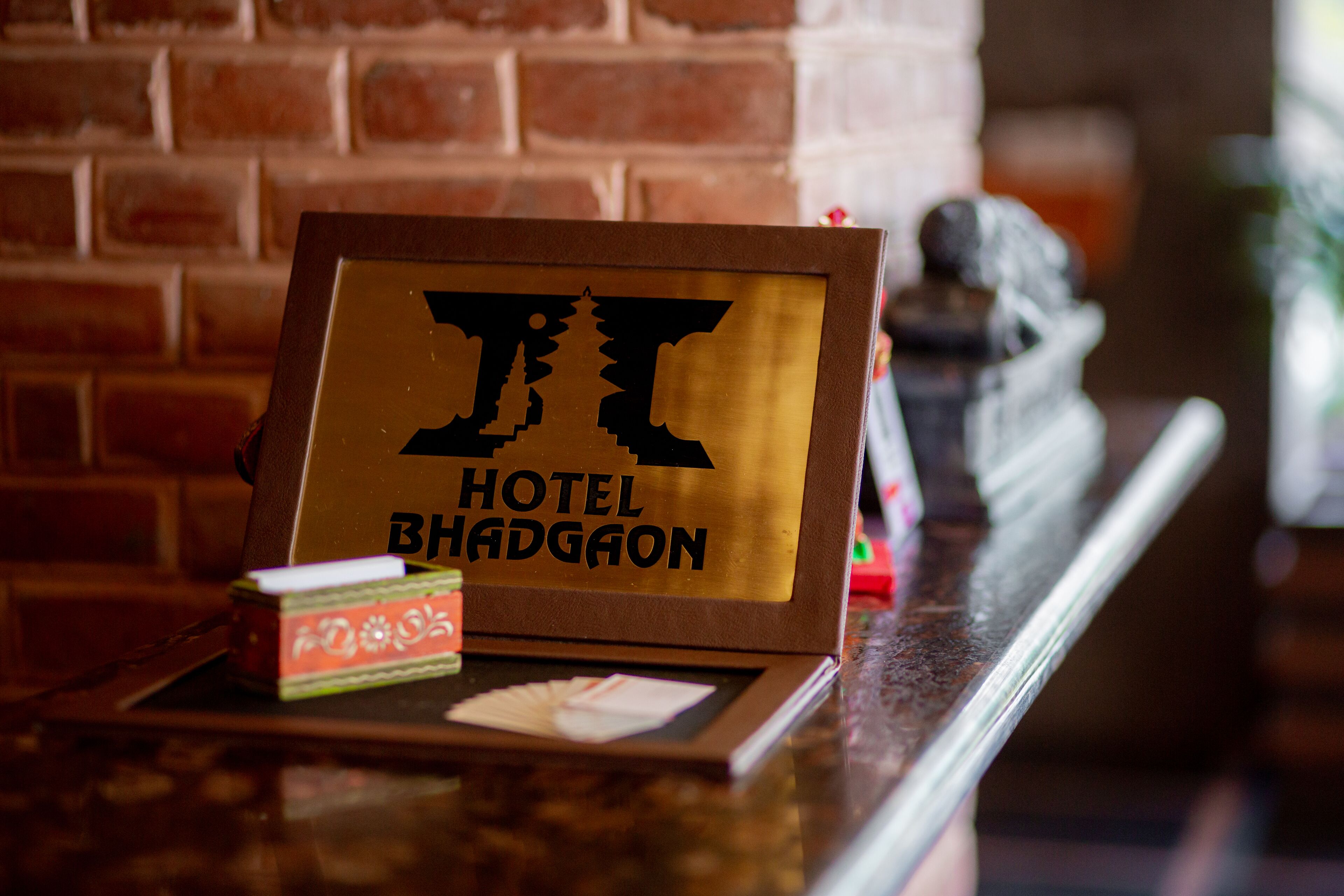 Um letreiro emoldurado com o texto 'HOTEL BHADGAON' em cima de um balcão.