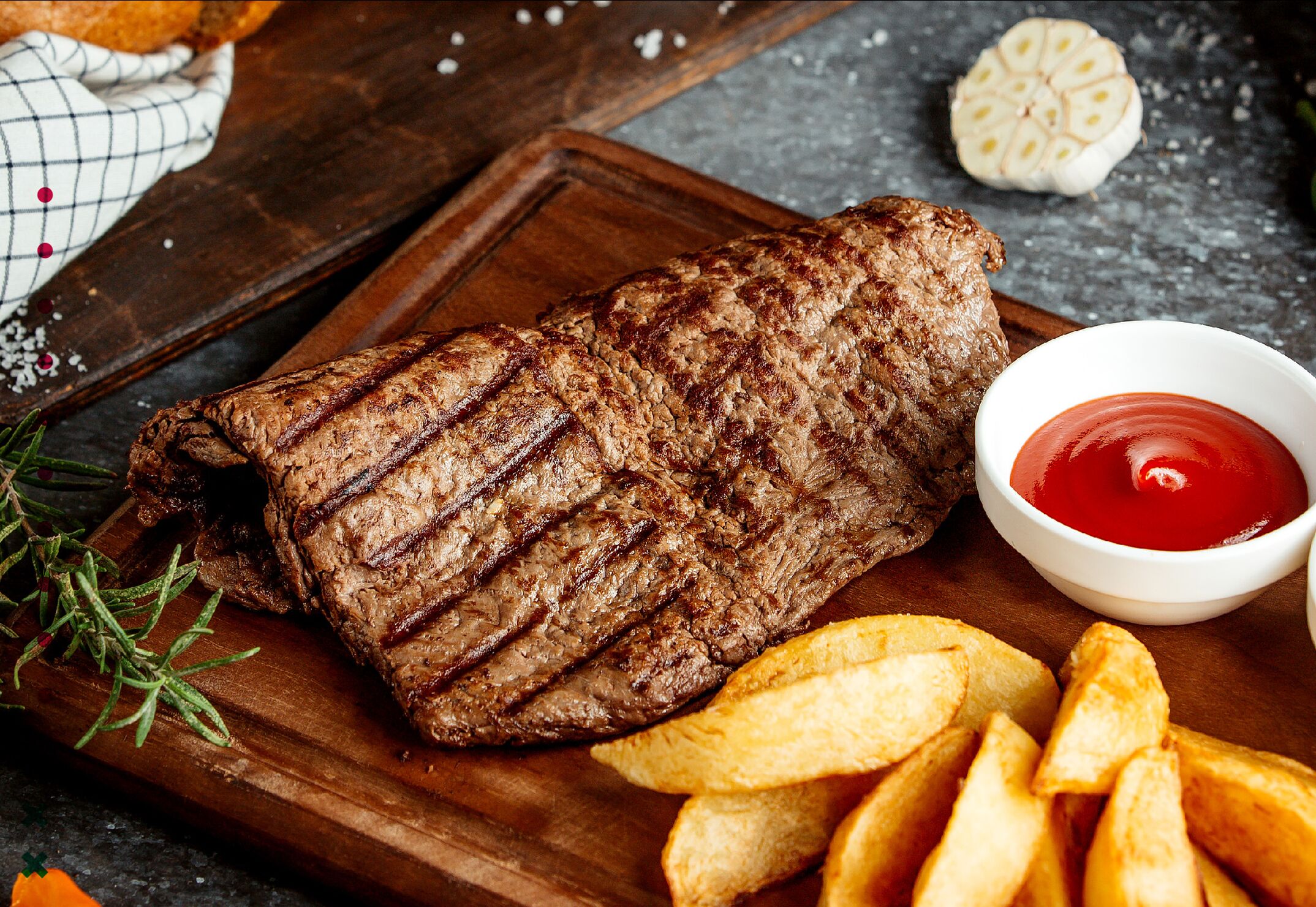 Bife grelhado com batatas fritas e ketchup em uma tábua de madeira.