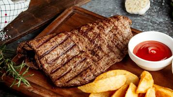 Bife grelhado com batatas fritas e ketchup em uma tábua de madeira.
