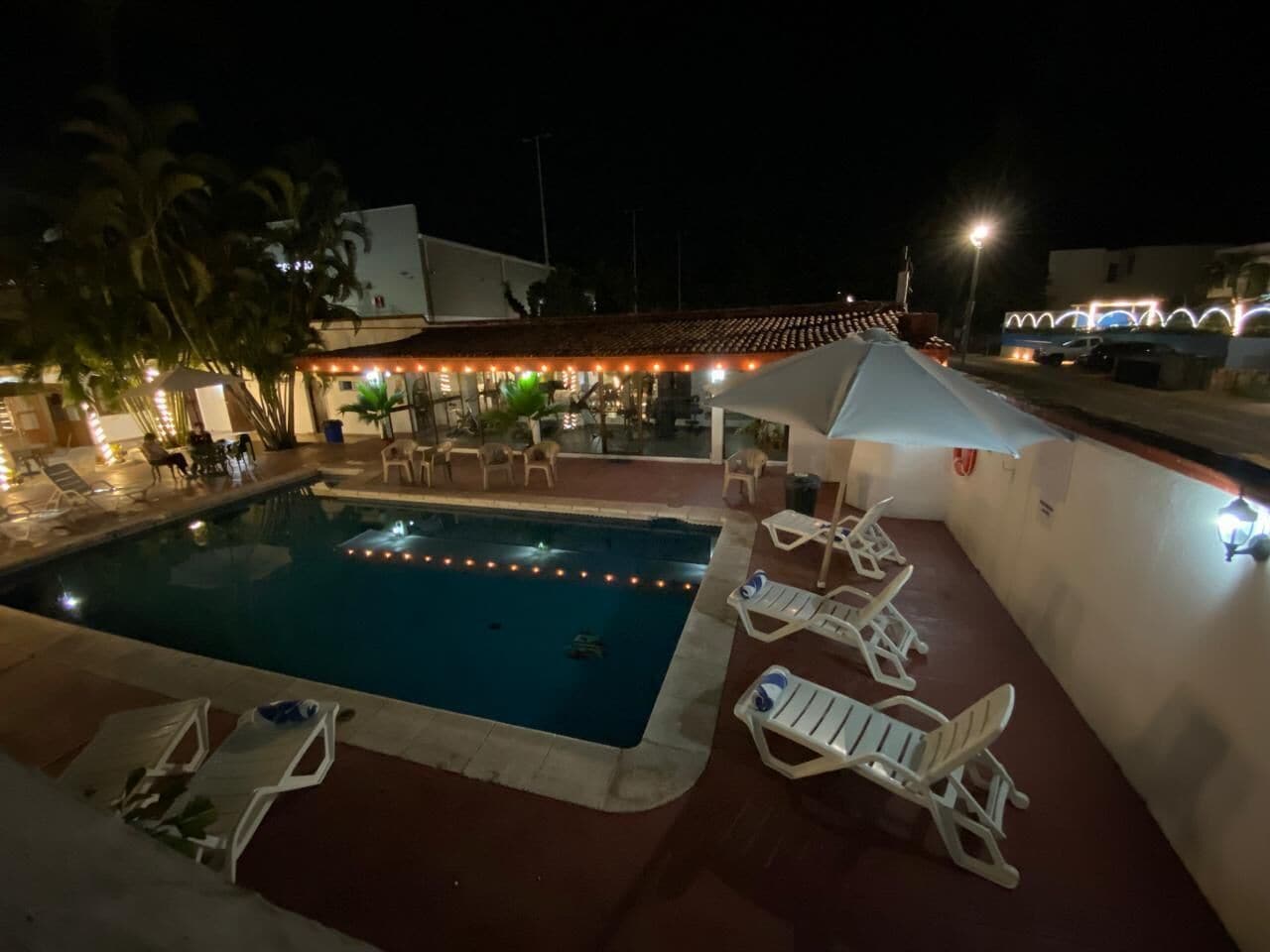 Uma piscina cercada por cadeiras de descanso e luzes de corda.