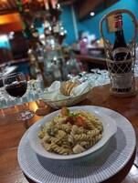 Uma mesa de jantar com um prato de massa, um copo de vinho tinto e uma garrafa de vinho numa cesta.