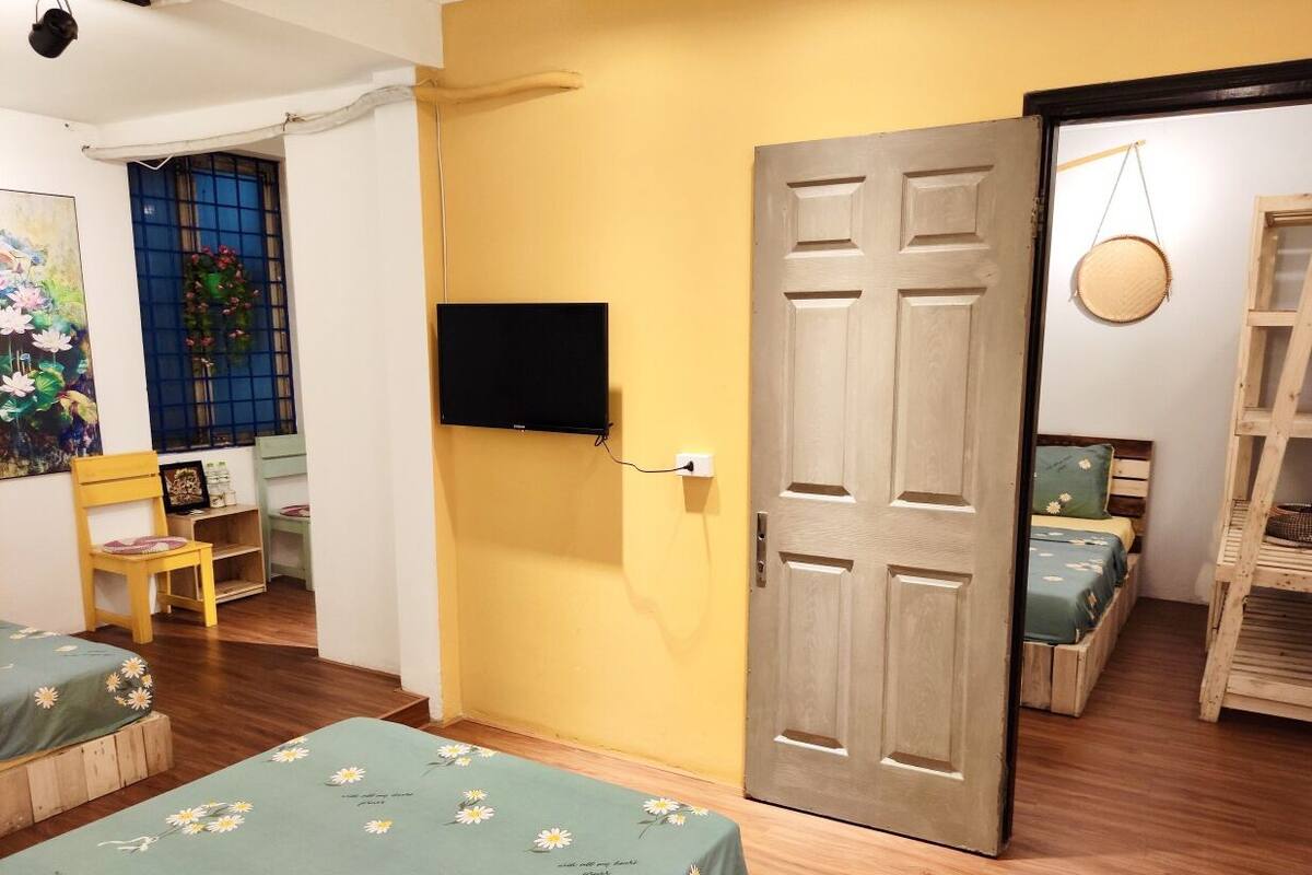 Quarto com uma cama, televisão na parede, porta de madeira e janela com moldura azul.