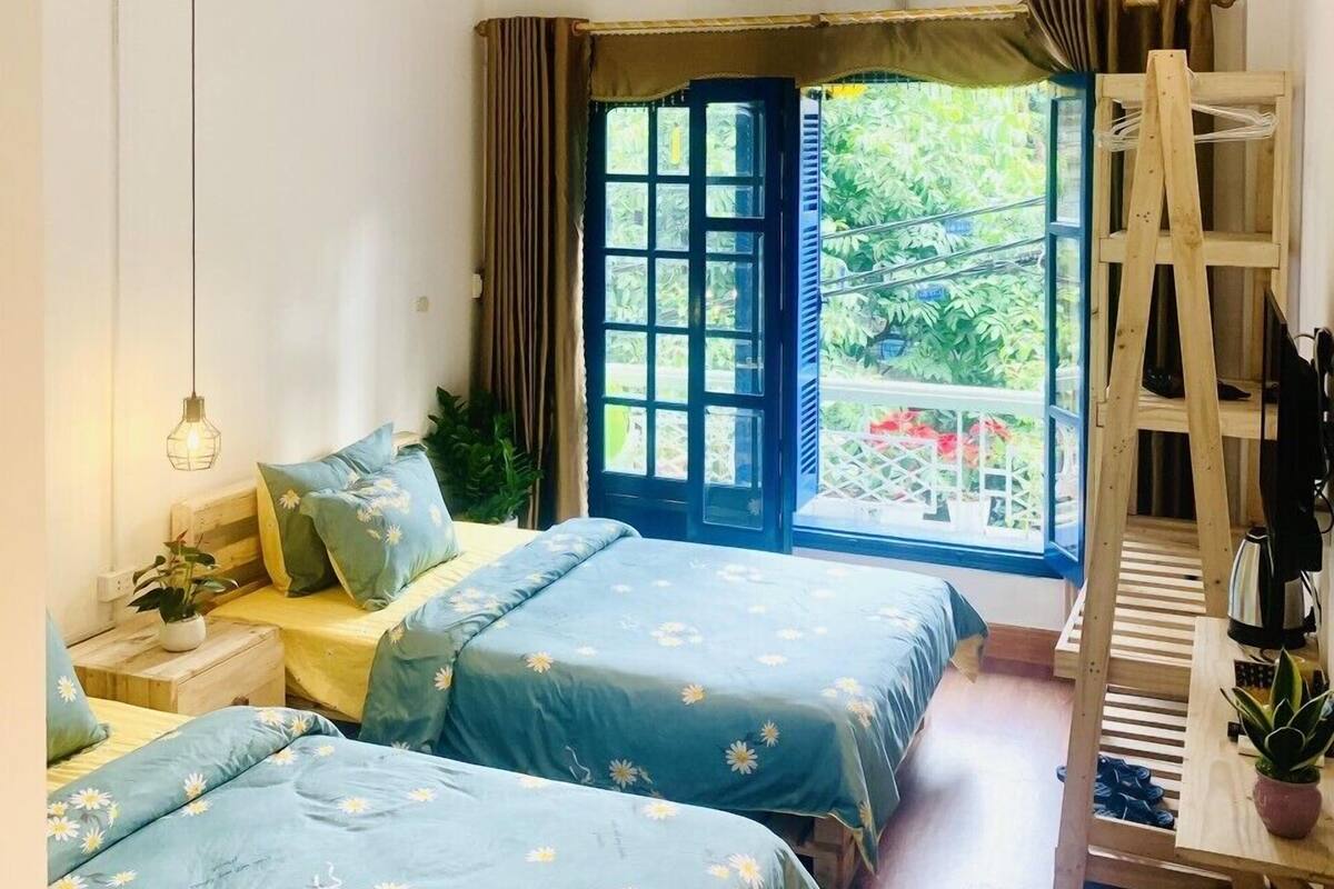Quarto com duas camas, ventilador de teto e janela com cortinas.