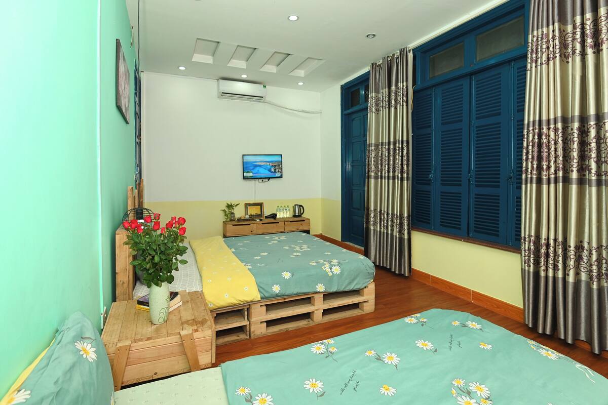 Quarto com cama, mesa de cabeceira, televisão e cortinas.