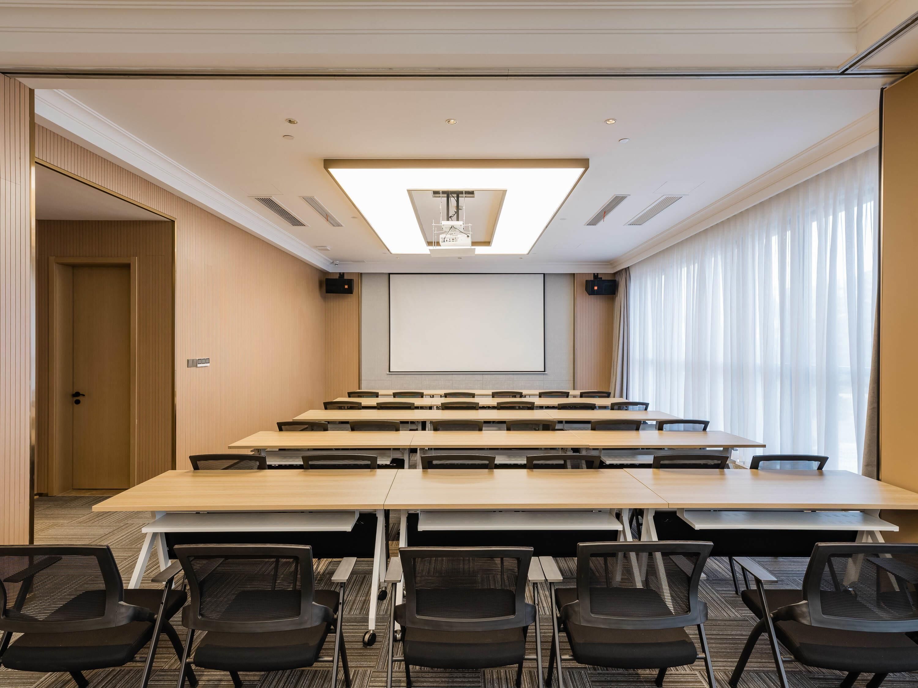Uma sala de conferências com uma mesa comprida, cadeiras, um projetor e um amplo janelão com cortinas.