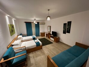 Quarto de hotel com duas camas de solteiro, um sofá, uma TV e uma pequena escrivaninha.