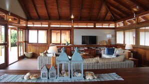Uma sala de estar ampla com teto de madeira alto, móveis de vime e uma televisão.