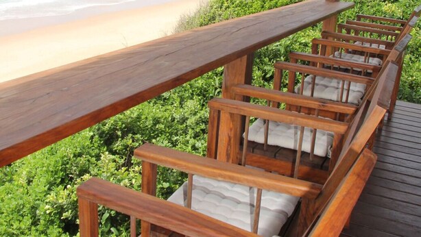 Um deck de madeira com cadeiras acolchoadas com vista para uma praia.