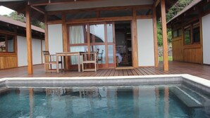 Uma área externa coberta com piscina, deck de madeira e um espaço de estar com mesa e cadeiras.