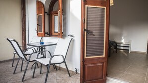 Uma área de refeições com mesa e cadeiras, uma porta de madeira com mosquiteiro e piso de azulejos.