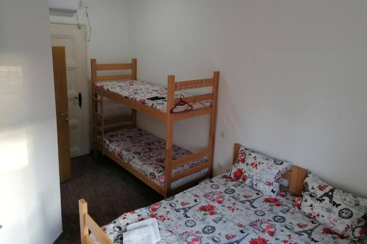 Quarto com beliches e uma cama de solteiro, paredes brancas e uma porta.