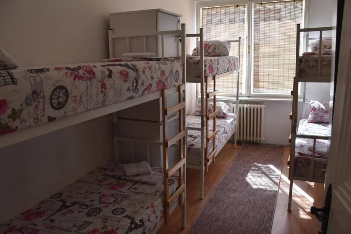 Quarto tipo dormitório com beliches, radiador e janela com persianas.