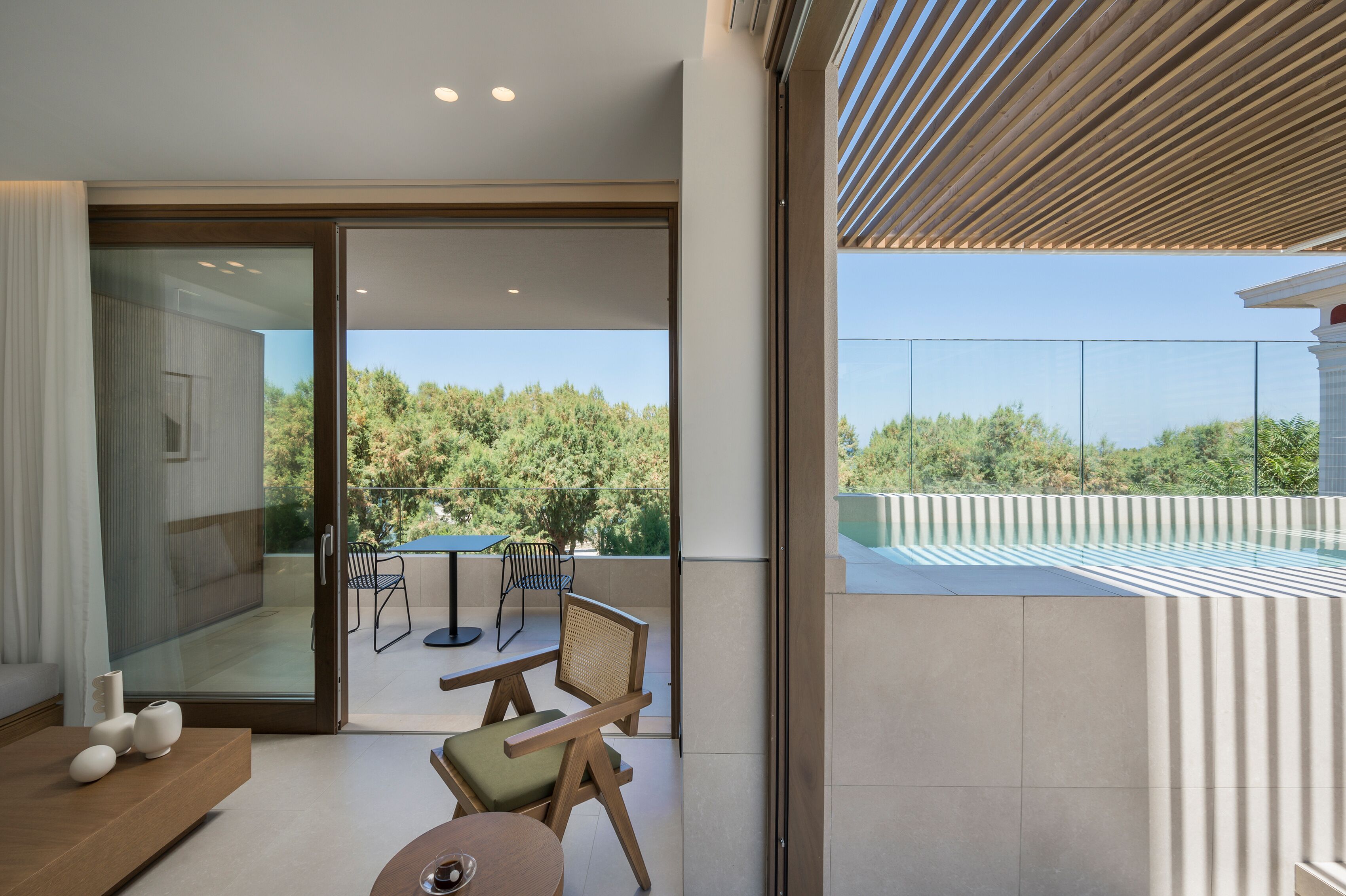 Varanda moderna com porta de vidro que dá para área de estar com mesa e cadeiras, com vista para paisagem verde exuberante.