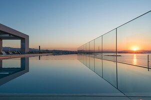 Uma piscina infinita moderna com guarda-vidro de vidro e vista para o pôr do sol sobre a água.