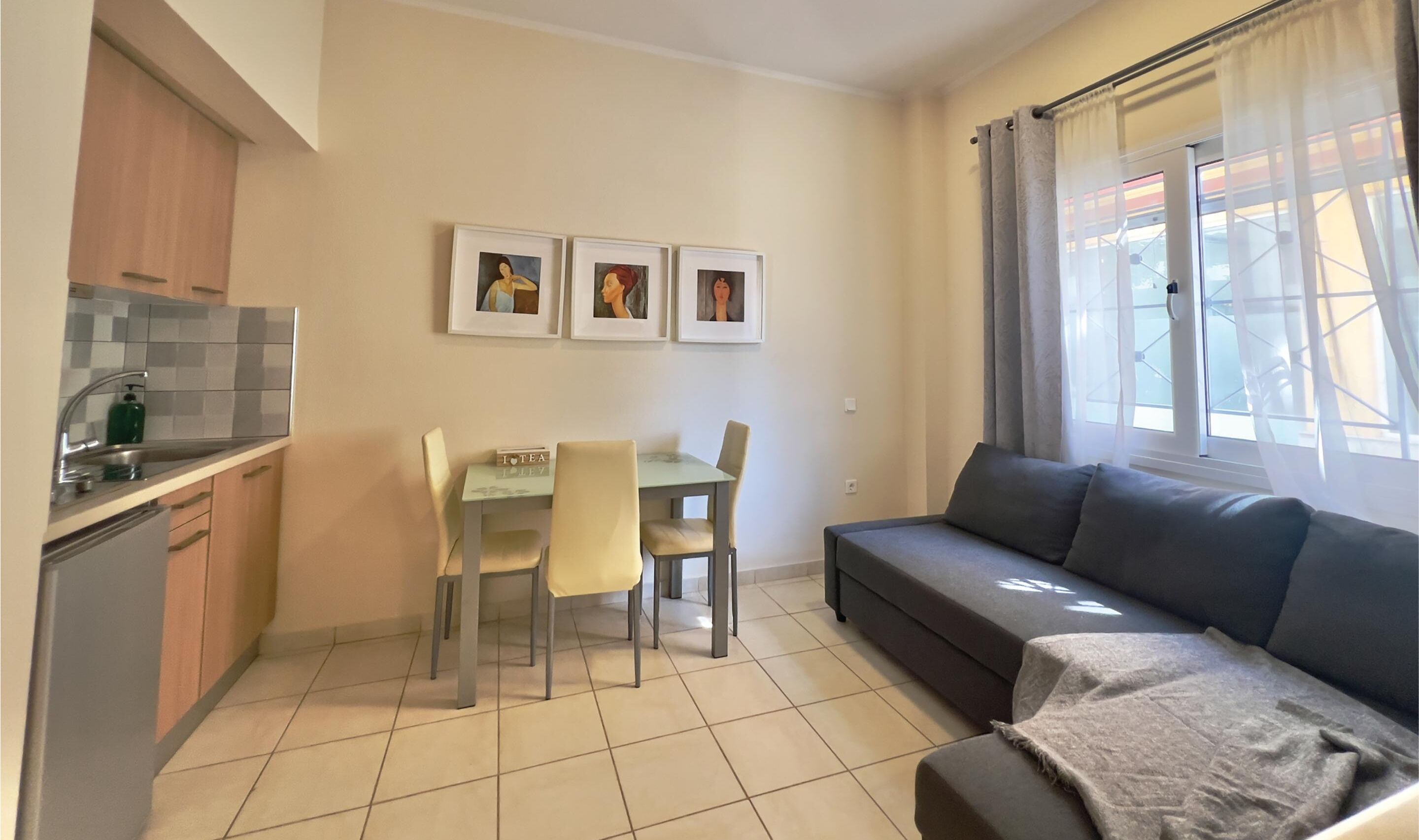 Um espaço de estar compacto com cozinha compacta, uma mesa de jantar com cadeiras, um sofá e três quadros na parede.
