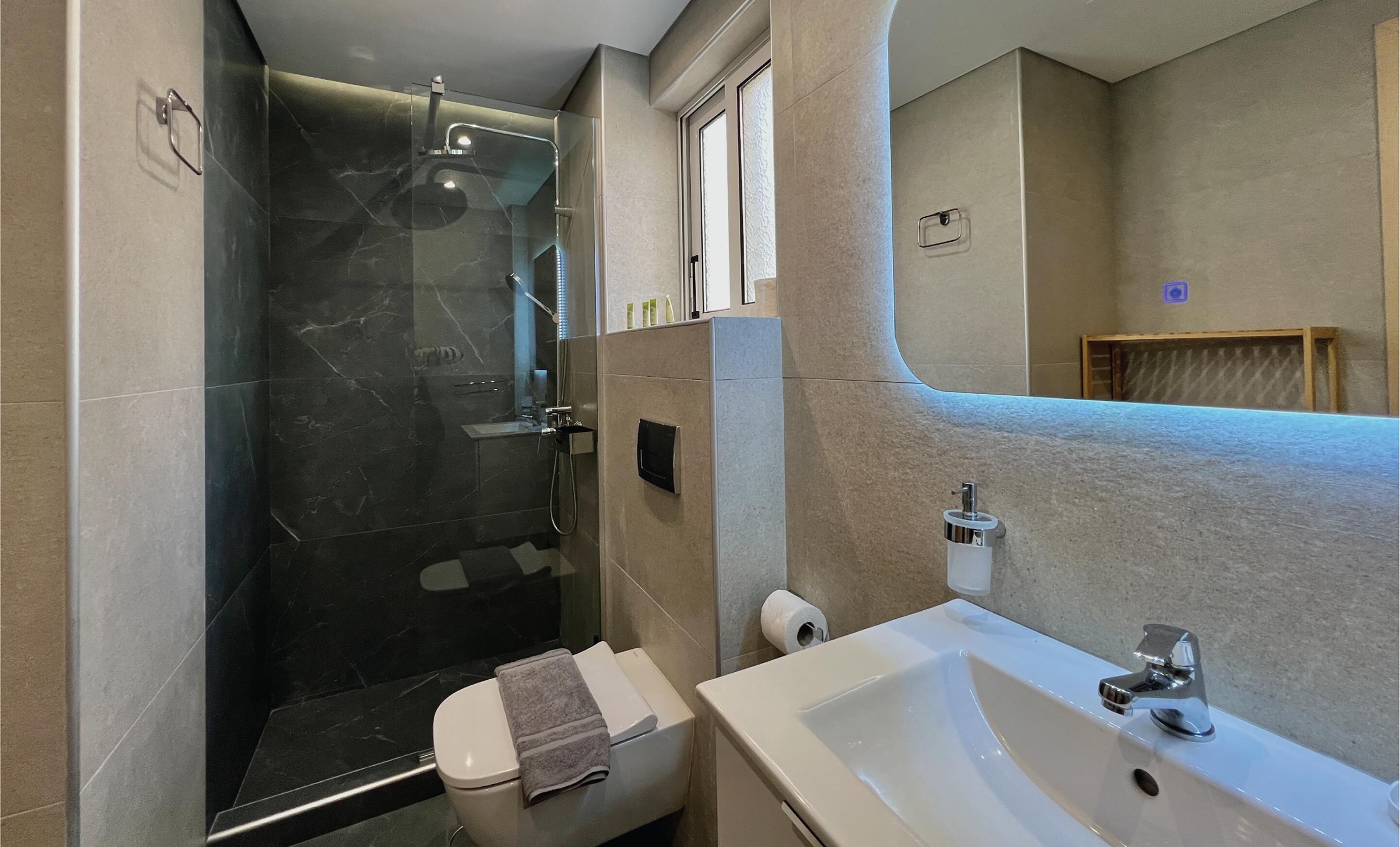 Casa de banho moderna com chuveiro envidraçado, sanita com toalha e lavatório com espelho.