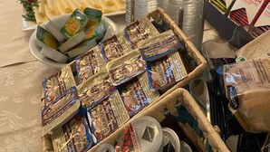 Uma mesa de buffet com diversos alimentos, incluindo doces, carnes, queijos e lanches embalados.