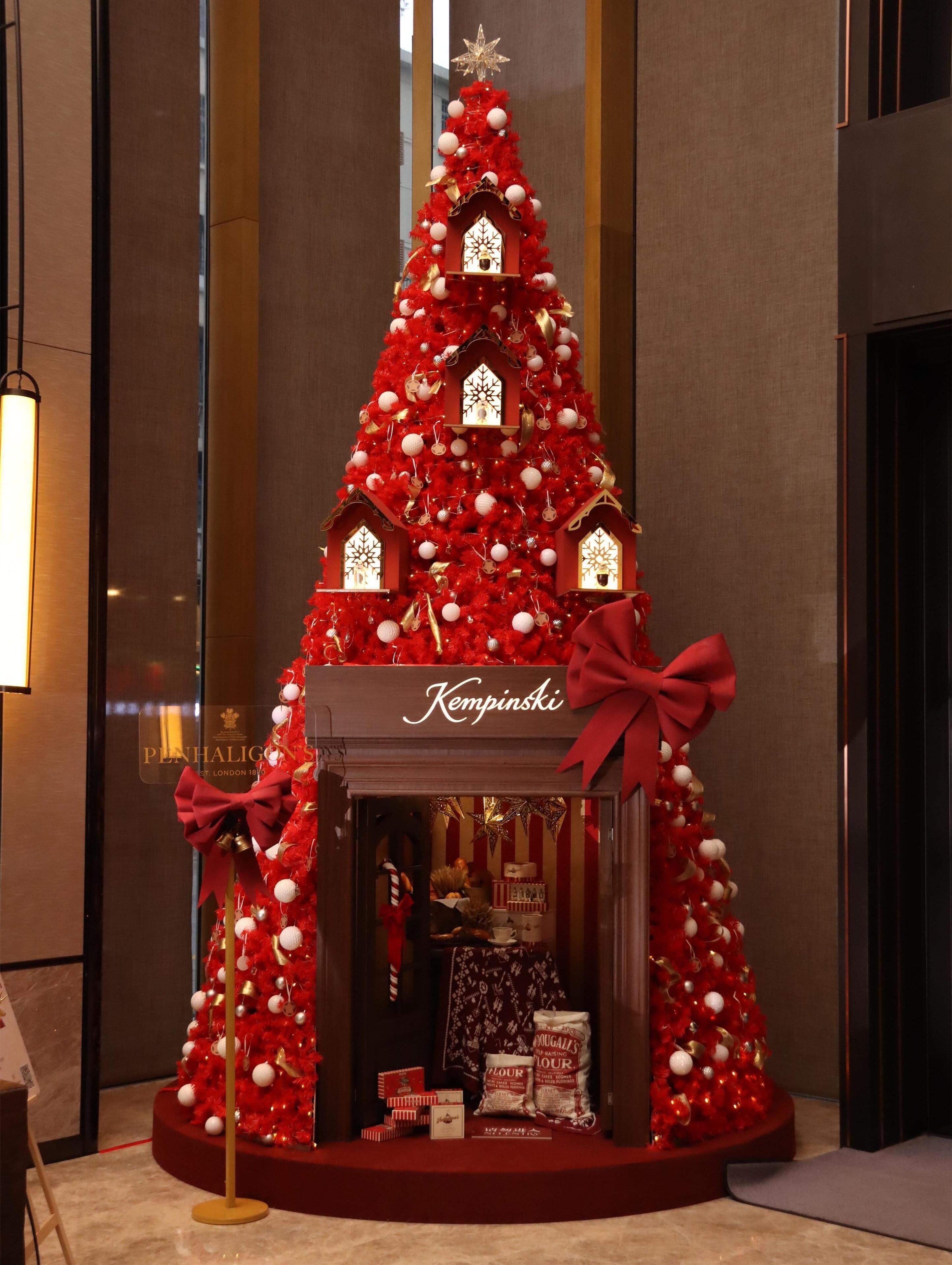 Decoração de Natal com uma árvore vermelha, uma loja chamada "Kempinski" e várias enfeites festivos.