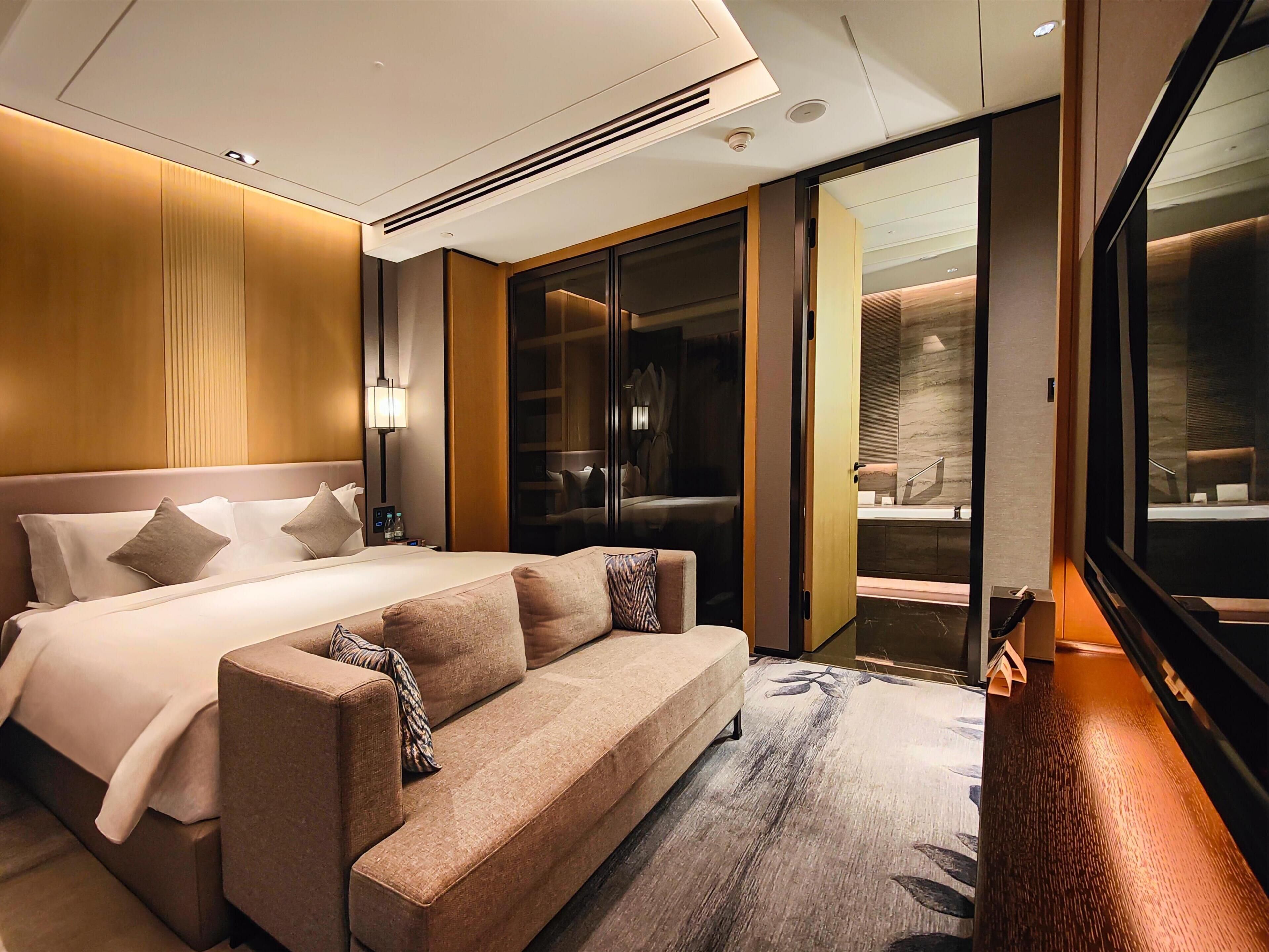 Quarto de hotel moderno com uma cama grande, um sofá, um closet espaçoso e um banheiro com banheira.