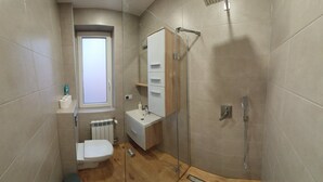 Casa de banho compacta com sanita, lavatório e cabine de duche com paredes de vidro.