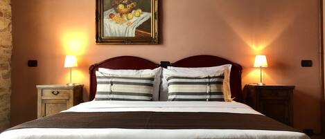 Quarto de hotel com cama, duas mesas de cabeceira, um criado-mudo, abajur e um quadro emoldurado na parede.