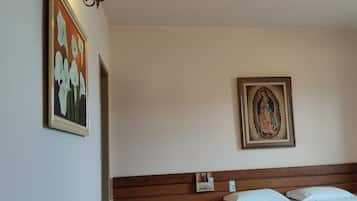 Quarto com cabeceira de madeira, cama com roupa de cama branca, mesa de cabeceira com abajur e duas fotos emolduradas na parede.