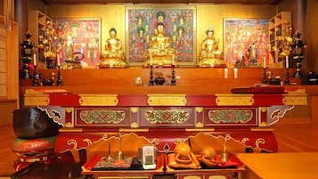 Quarto tradicional com altar de madeira, estátuas douradas e pinturas religiosas.