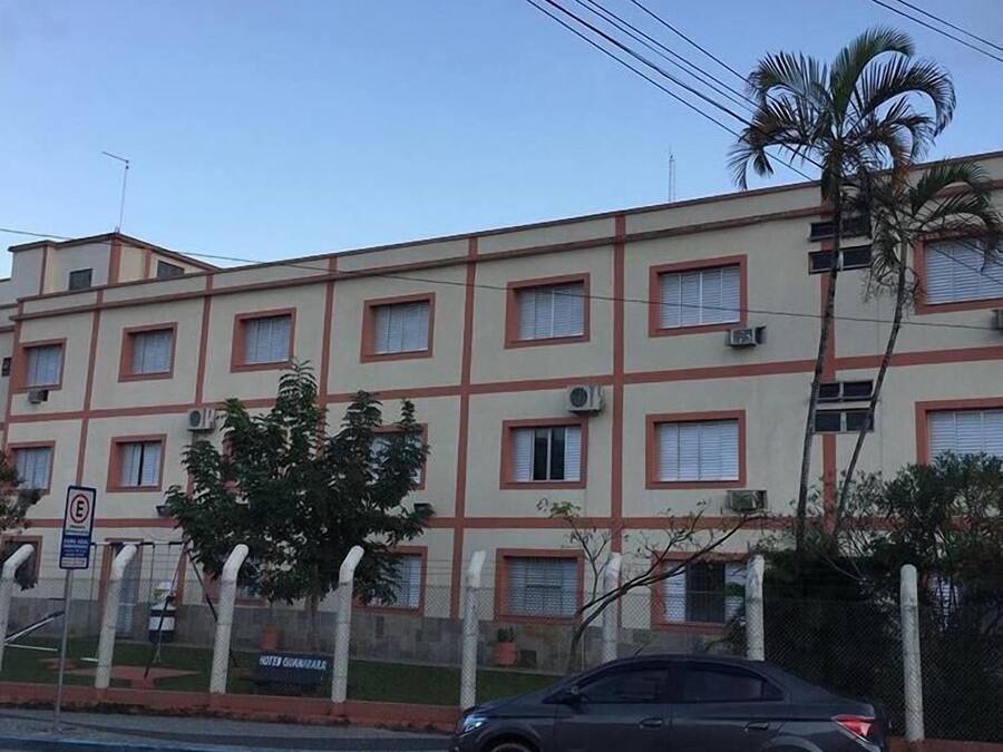 Hotel de vários andares, com uma fileira de janelas e placa indicando área proibida para estacionamento.