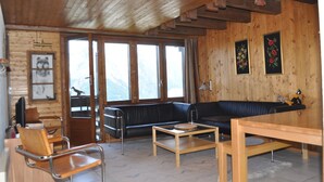 Interior acolhedor de cabana com teto de madeira, sofá de couro preto, mesa de centro de madeira e mesa de jantar de madeira.