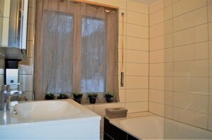 Um banheiro moderno com uma banheira grande, uma janela com cortinas e plantas em vasos no parapeito.