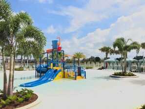 Um parque aquático com uma estrutura de recreação azul e amarela, palmeiras e um céu claro.