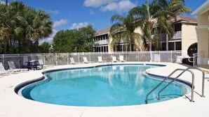 Piscina com espreguiçadeiras e palmeiras, cercada por um muro branco.