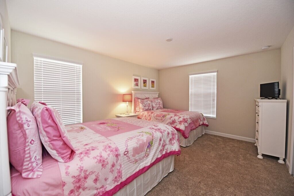 Quarto com duas camas, paredes brancas, carpete bege e cômoda branca.