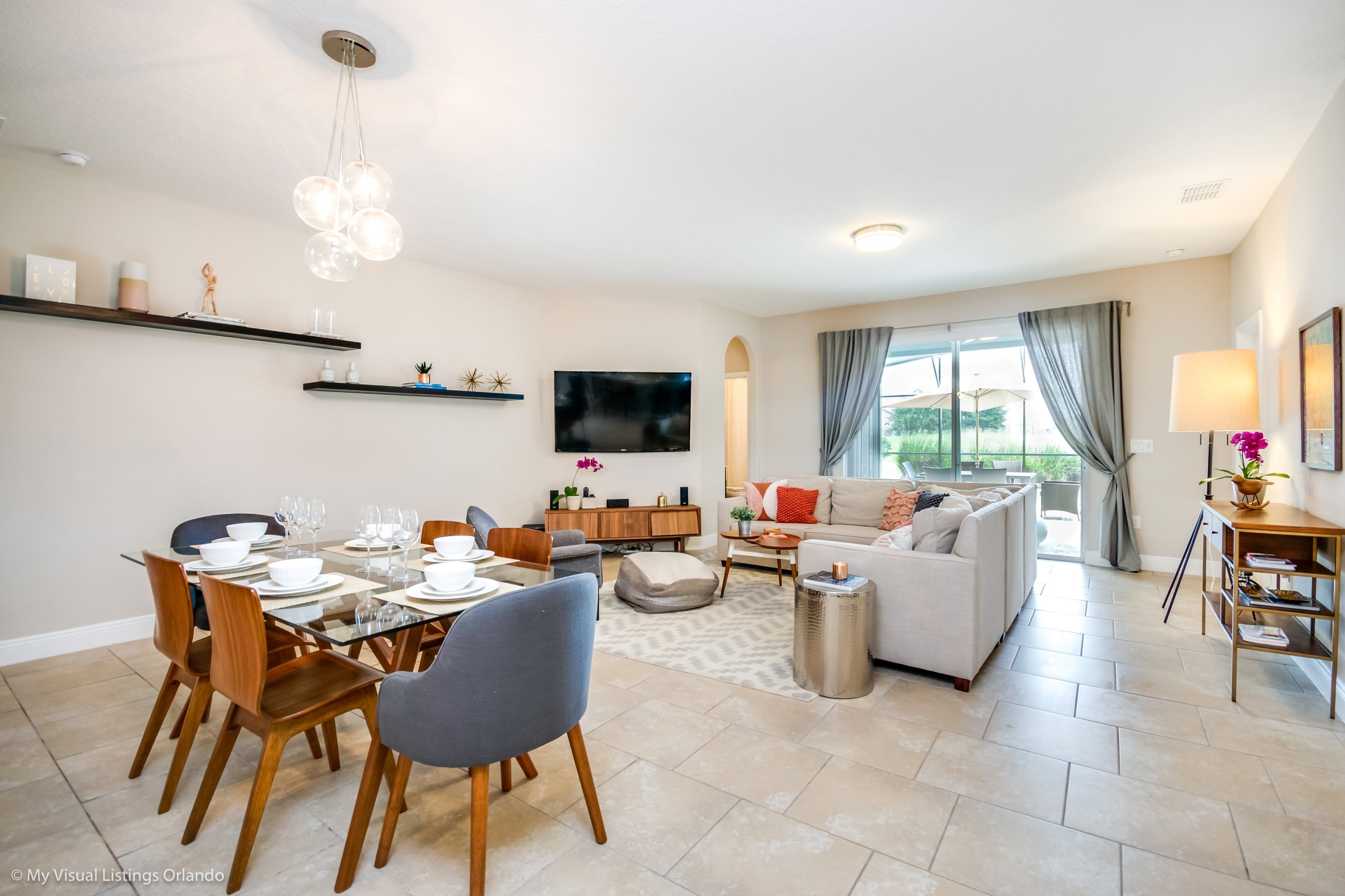 Uma sala de estar moderna com área de jantar, um conjunto de sofá e uma TV na parede.