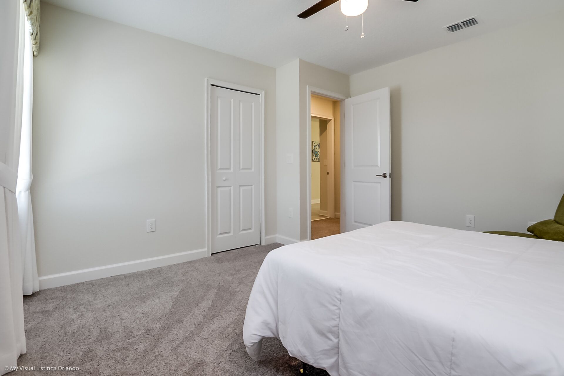 Quarto com cama, piso coberto por carpete, paredes brancas e ventilador de teto.