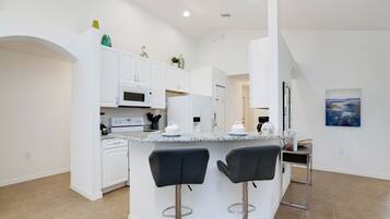 Cozinha moderna com armários brancos, uma ilha central com dois banquetes e um quadro na parede.