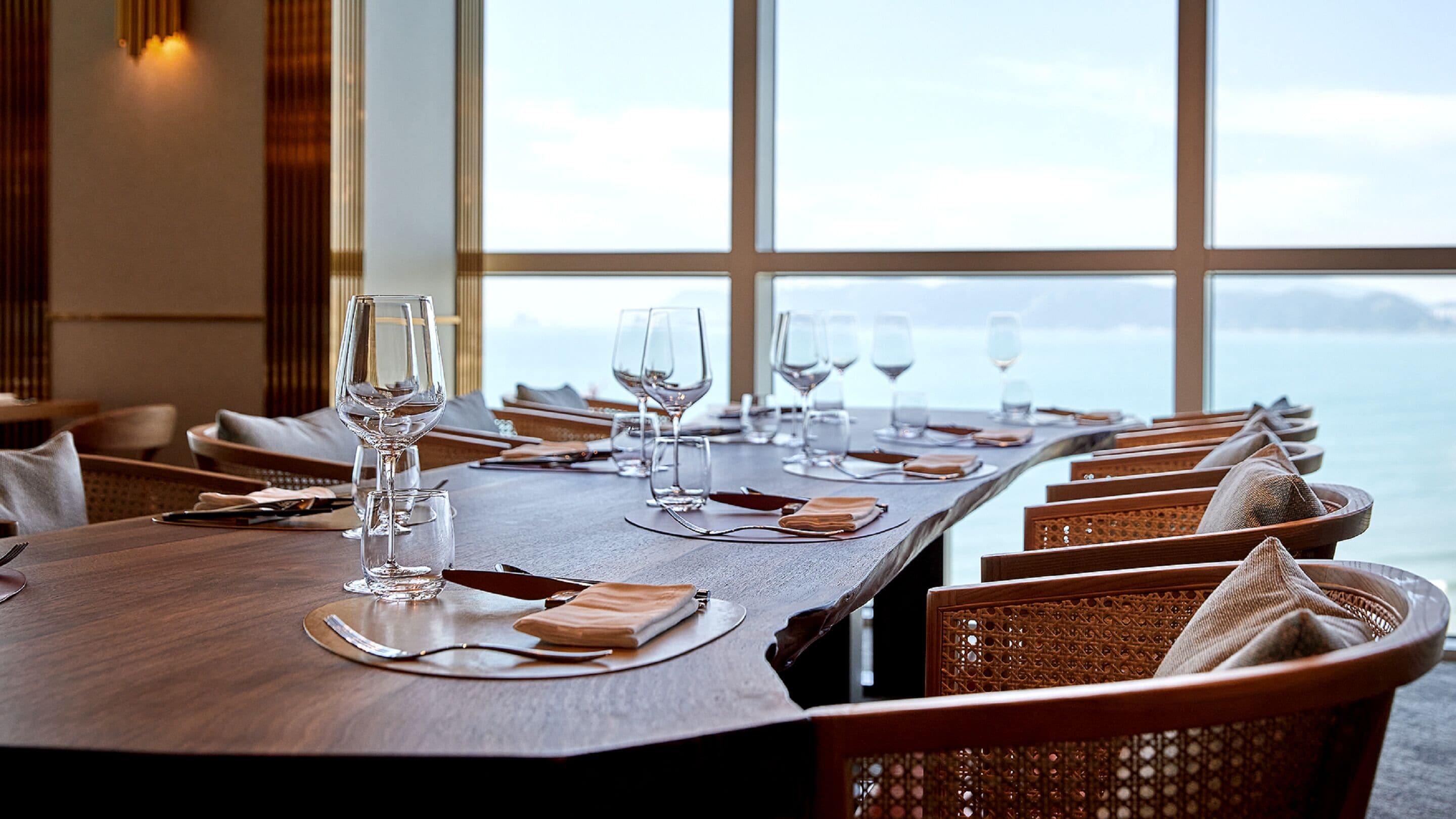 Mesa de jantar posta para refeição, com taças de vinho, talheres e guardanapos, com vista panorâmica.