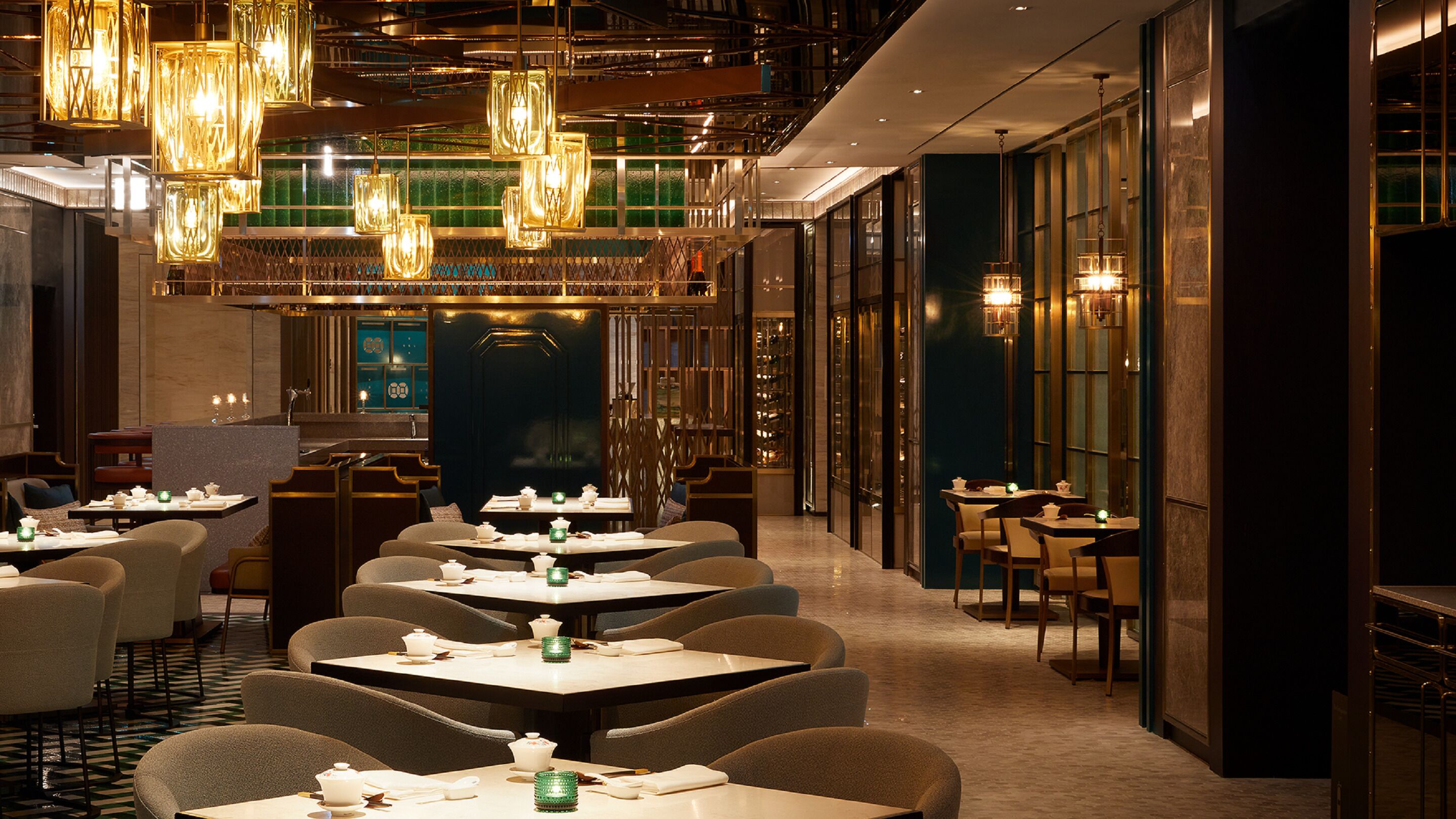 Interior moderno de restaurante com várias mesas e cadeiras, iluminação acolhedora e vista da cidade através de grandes janelas.