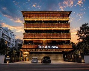 Um hotel de vários andares com design moderno, com uma entrada destacada e uma placa que diz 'The Ashoka'.