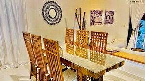 Uma área de refeições com uma mesa e cadeiras de madeira, um detalhe decorativo na parede e vista pela janela.
