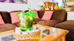 Uma sala de estar com um sofá marrom, uma mesa de centro de vidro e uma cesta de vime com objetos decorativos.