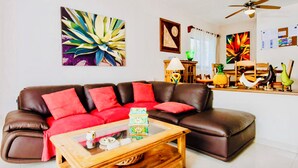 Sala de estar com sofá de couro marrom, almofadas vermelhas, mesa de centro de madeira e ventilador de teto.