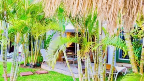 Um jardim exuberante com palmeiras, um espaço de varanda com móveis de exterior e um edifício com porta verde.