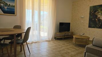 Uma sala de estar com uma mesa de jantar, cadeiras, uma televisão e um sofá.